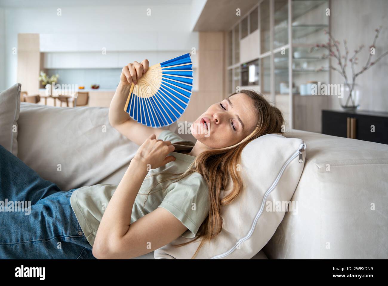 Exhausted woman lying on sofa waving with hand fan, suffering from ...