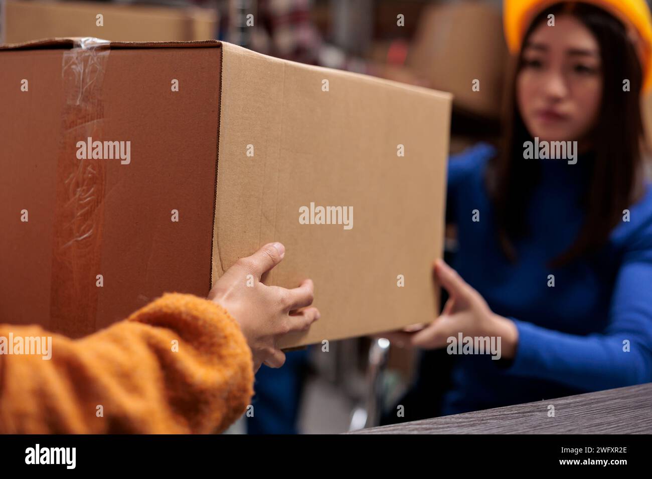 Postal service coworkers holding cardboard box in industrial warehouse ...