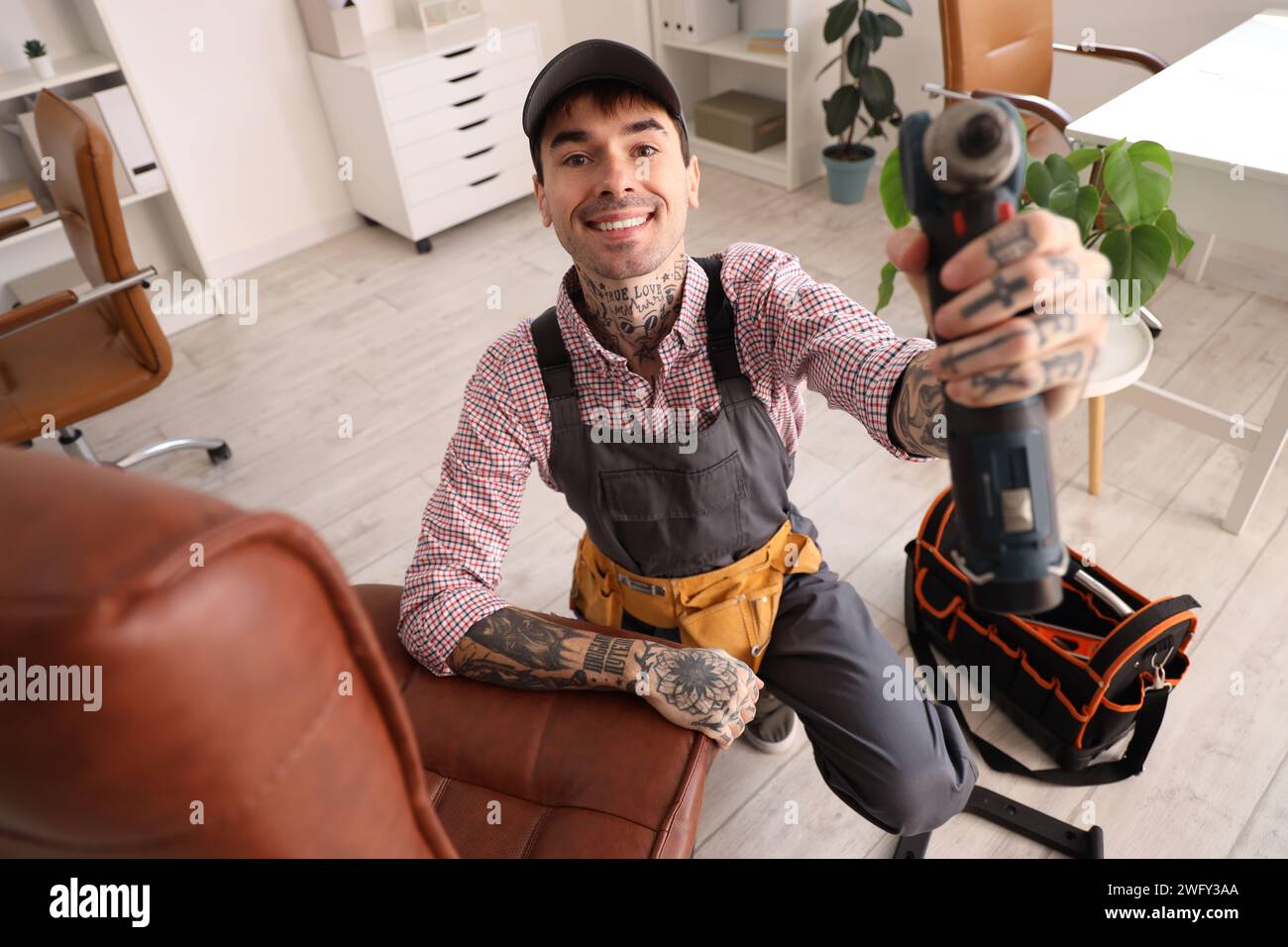 Male worker with drill assembling chair in office Stock Photo - Alamy