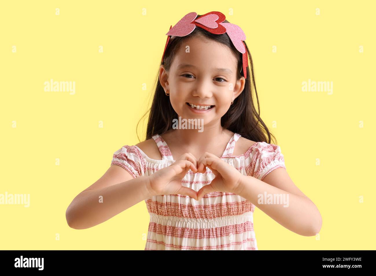 Cute little Asian girl making heart gesture on yellow background ...