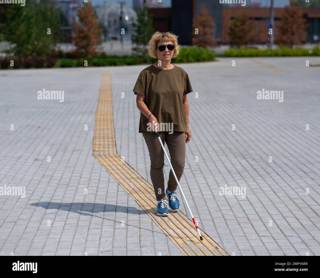 An elderly blind woman walks with a cane along a tactile tile Stock ...
