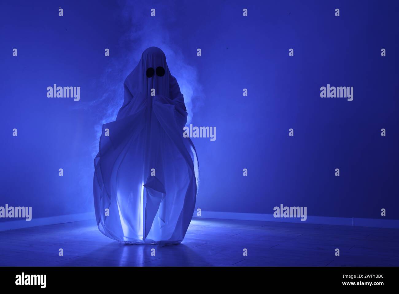 Creepy ghost. Woman covered with sheet in blue light, space for text ...