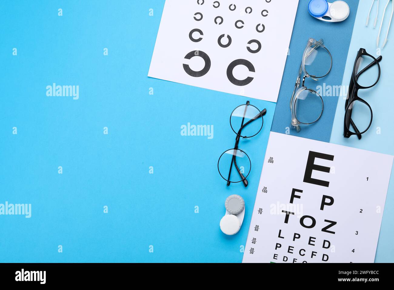 Vision test charts, glasses, lenses and tweezers on light blue ...