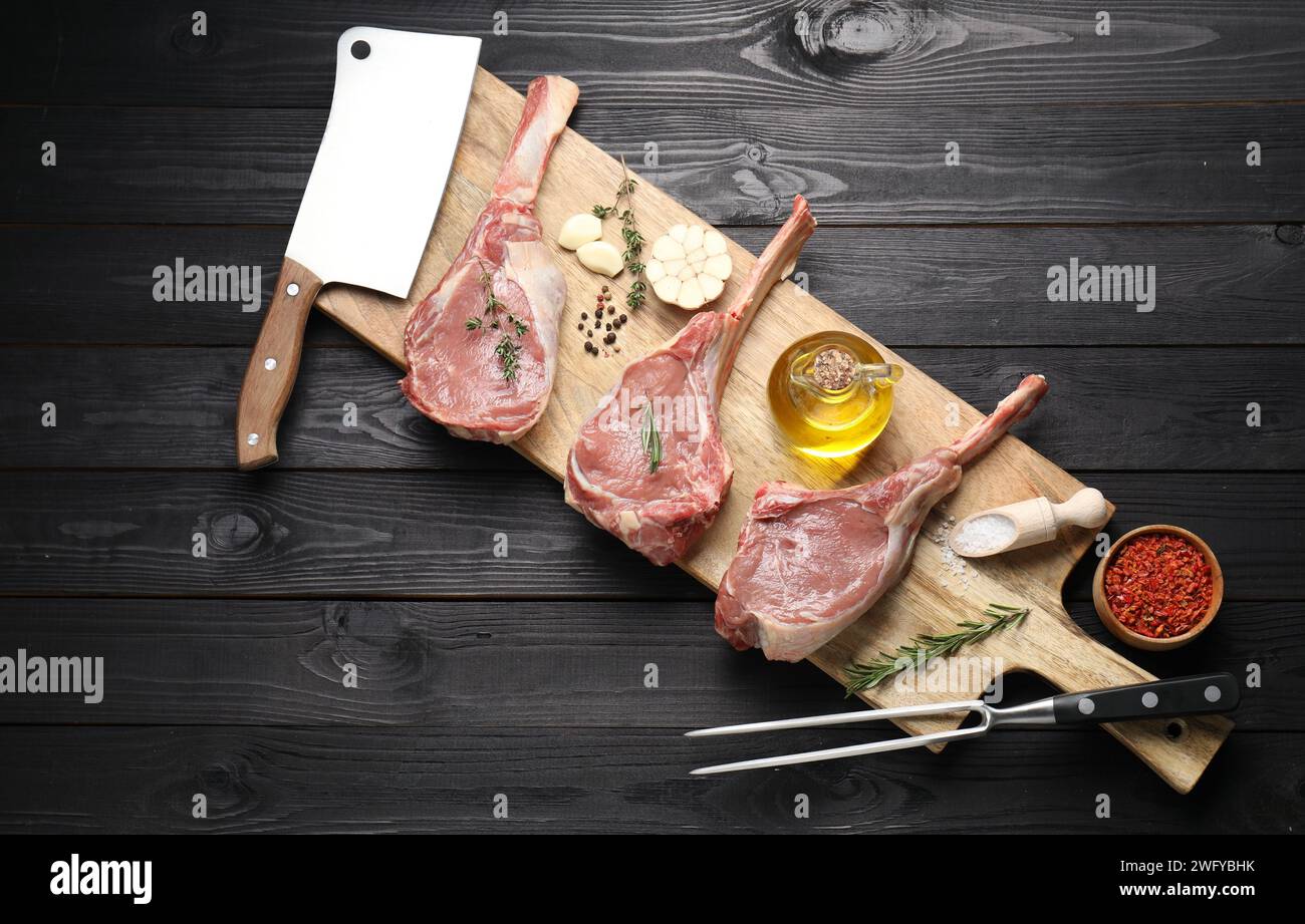 Fresh tomahawk beef cuts, spices and butcher tools on black wooden ...