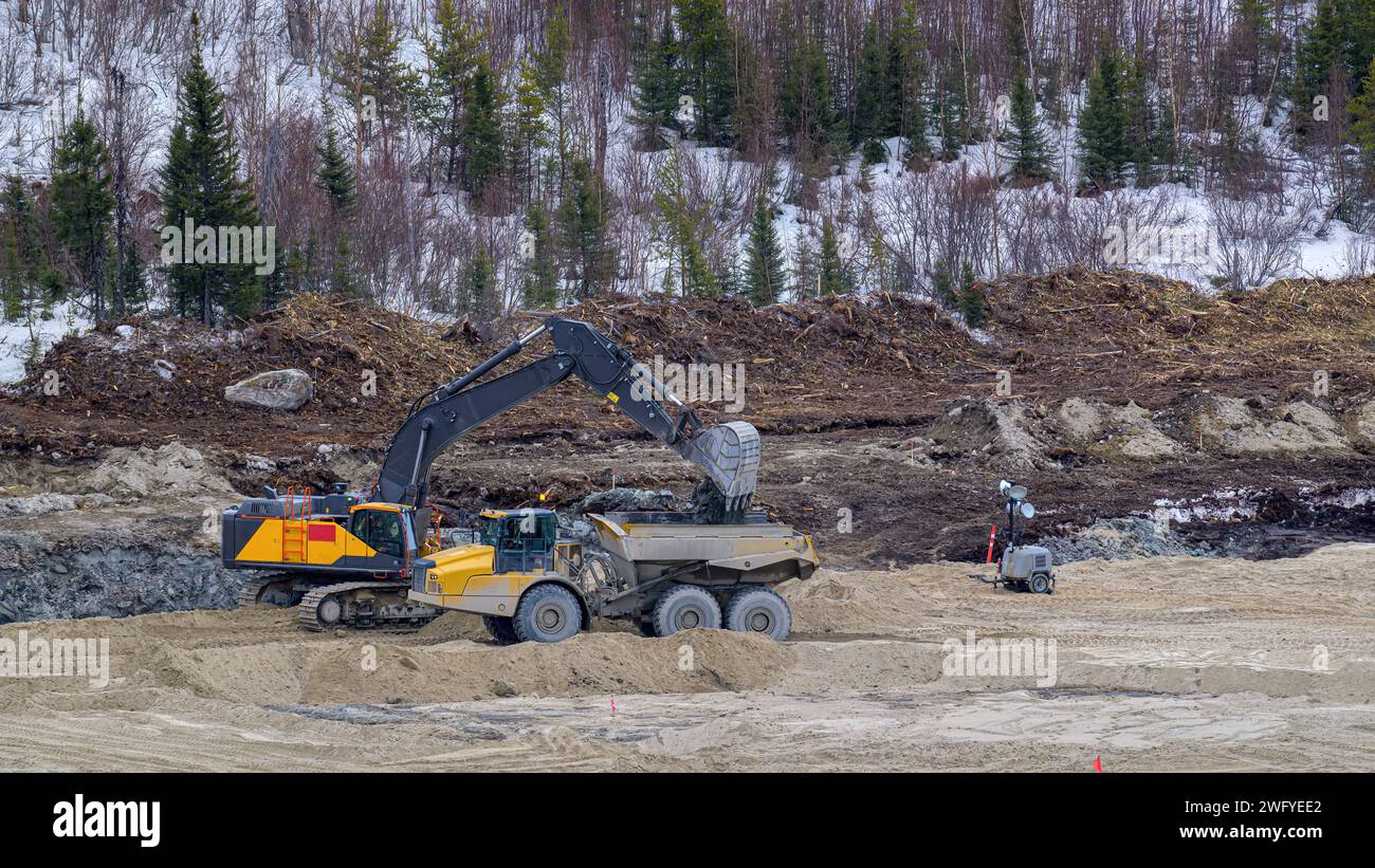 Excavator loading soil into a dumper at the foot of a hill in winter ...