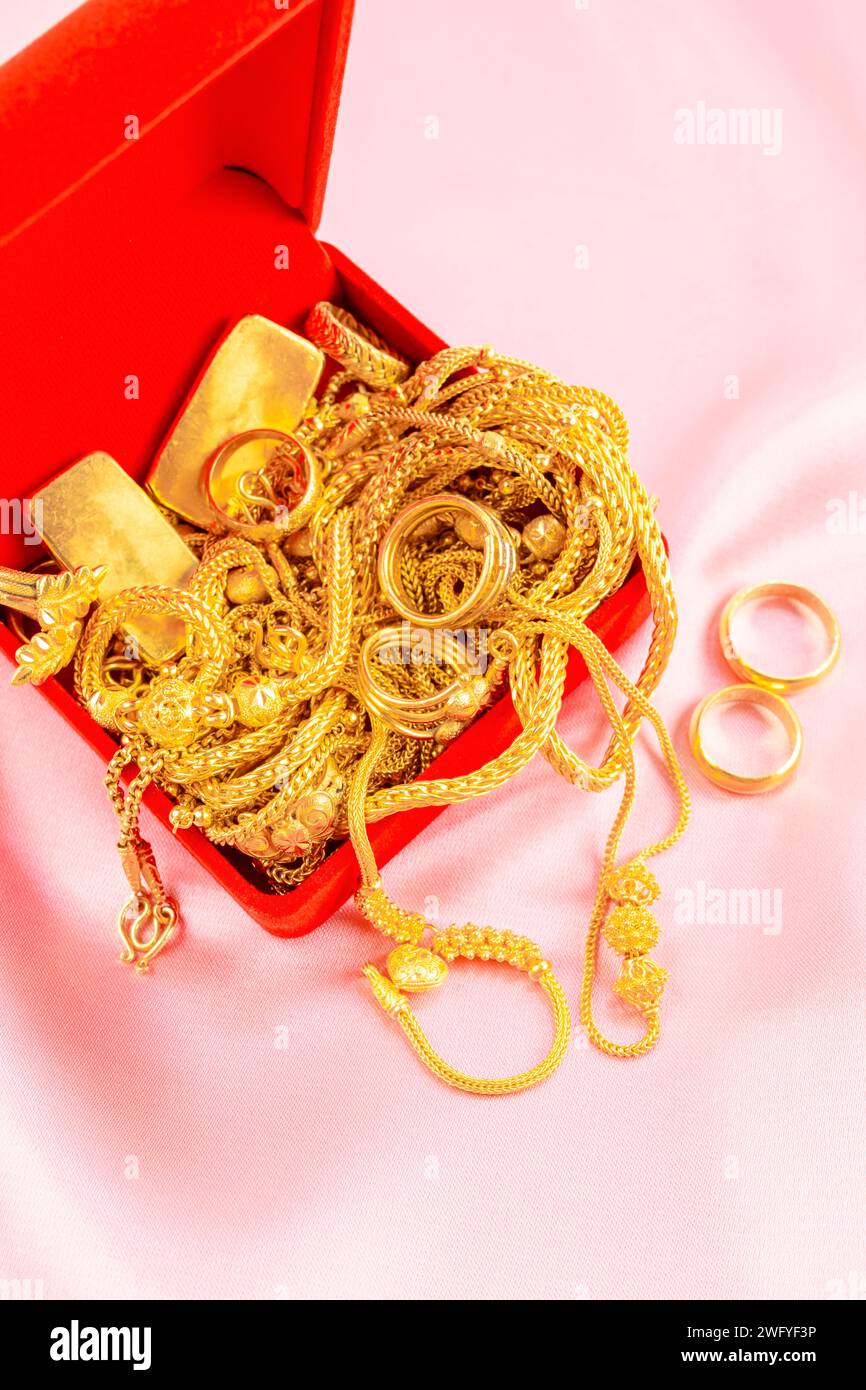 Many gold necklaces and gold bars in red box on pink velvet cloth ...