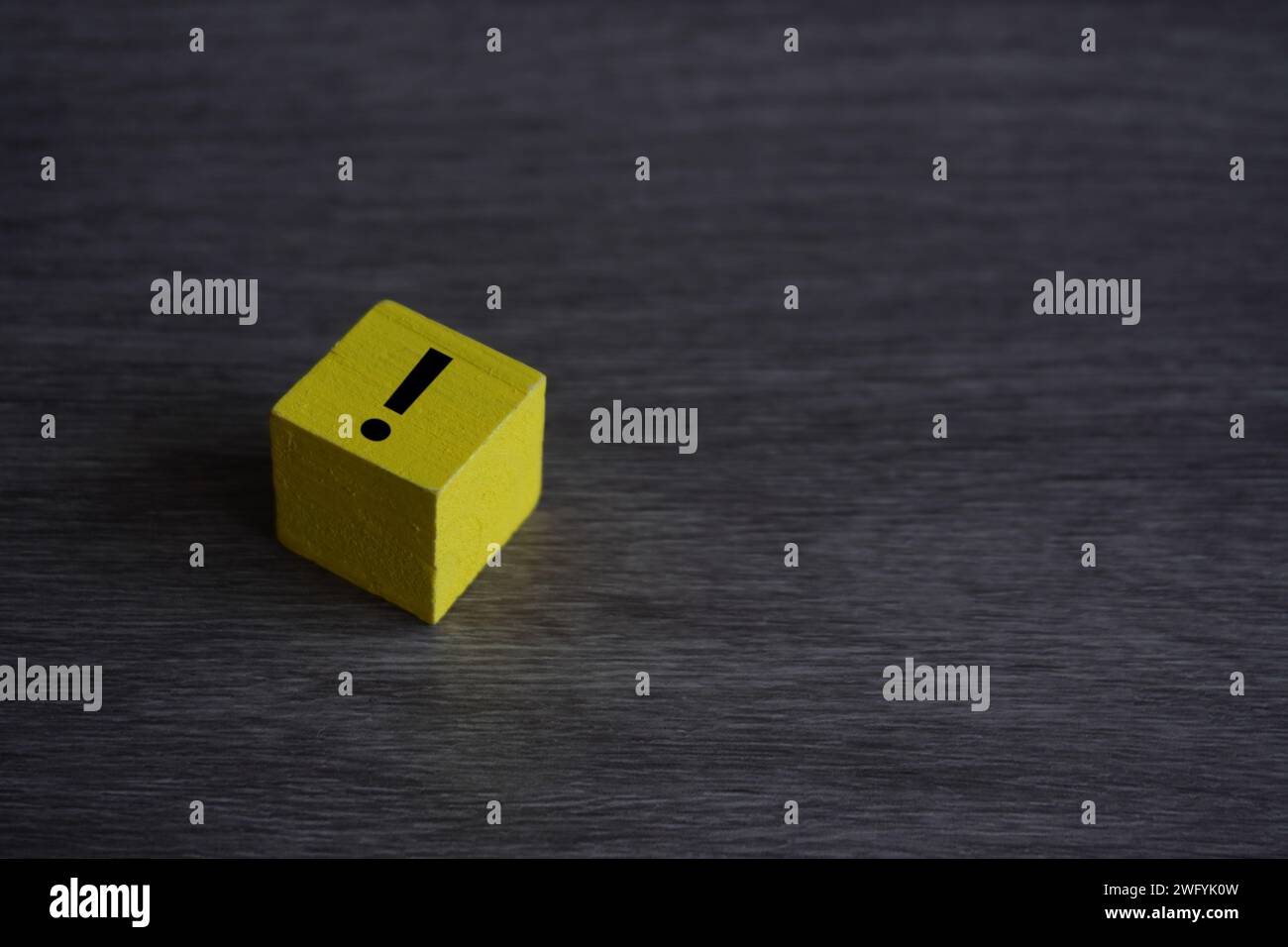 Yellow wooden cube on table with exclamation mark icon. Copy space for ...