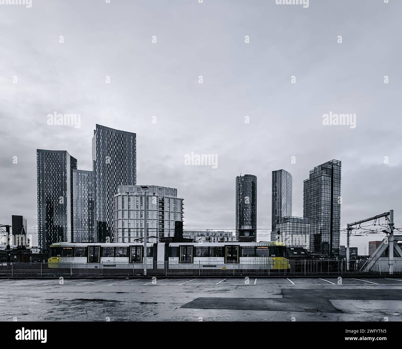 Bee Network tram in Manchester passing by the skyline of tall buildings ...