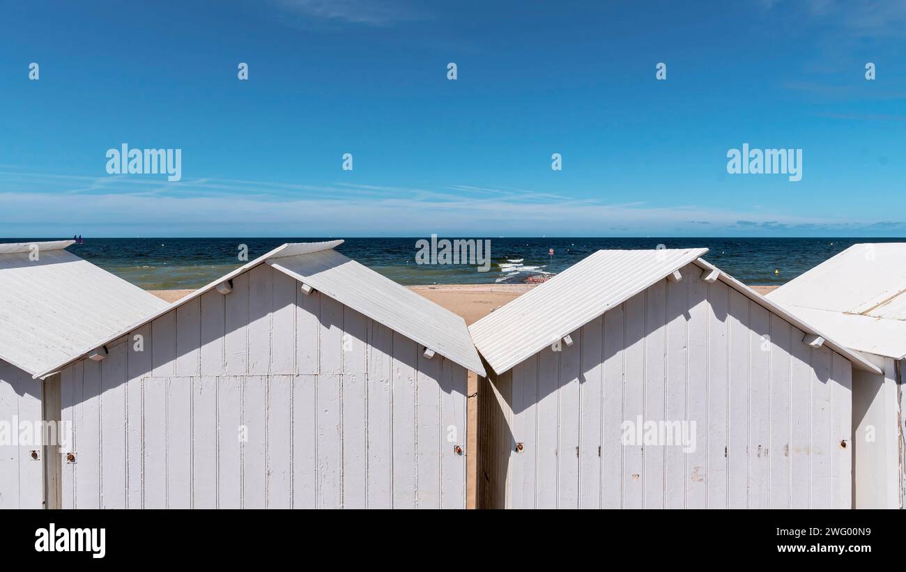 A row of colorful beach huts along the ocean with boats in the water ...