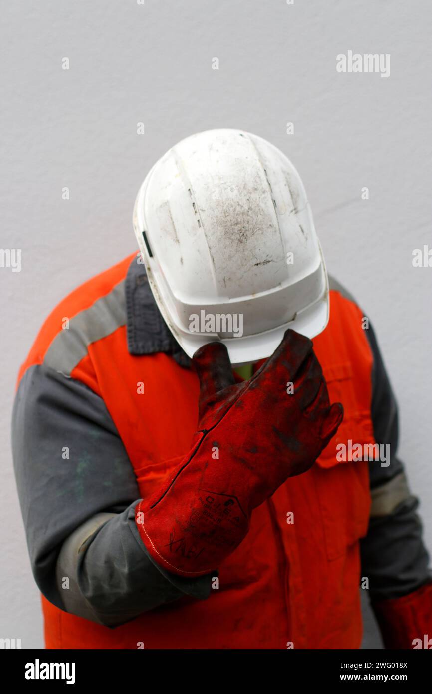 A tired worker after a shift in an orange jacket and helmet gently ...