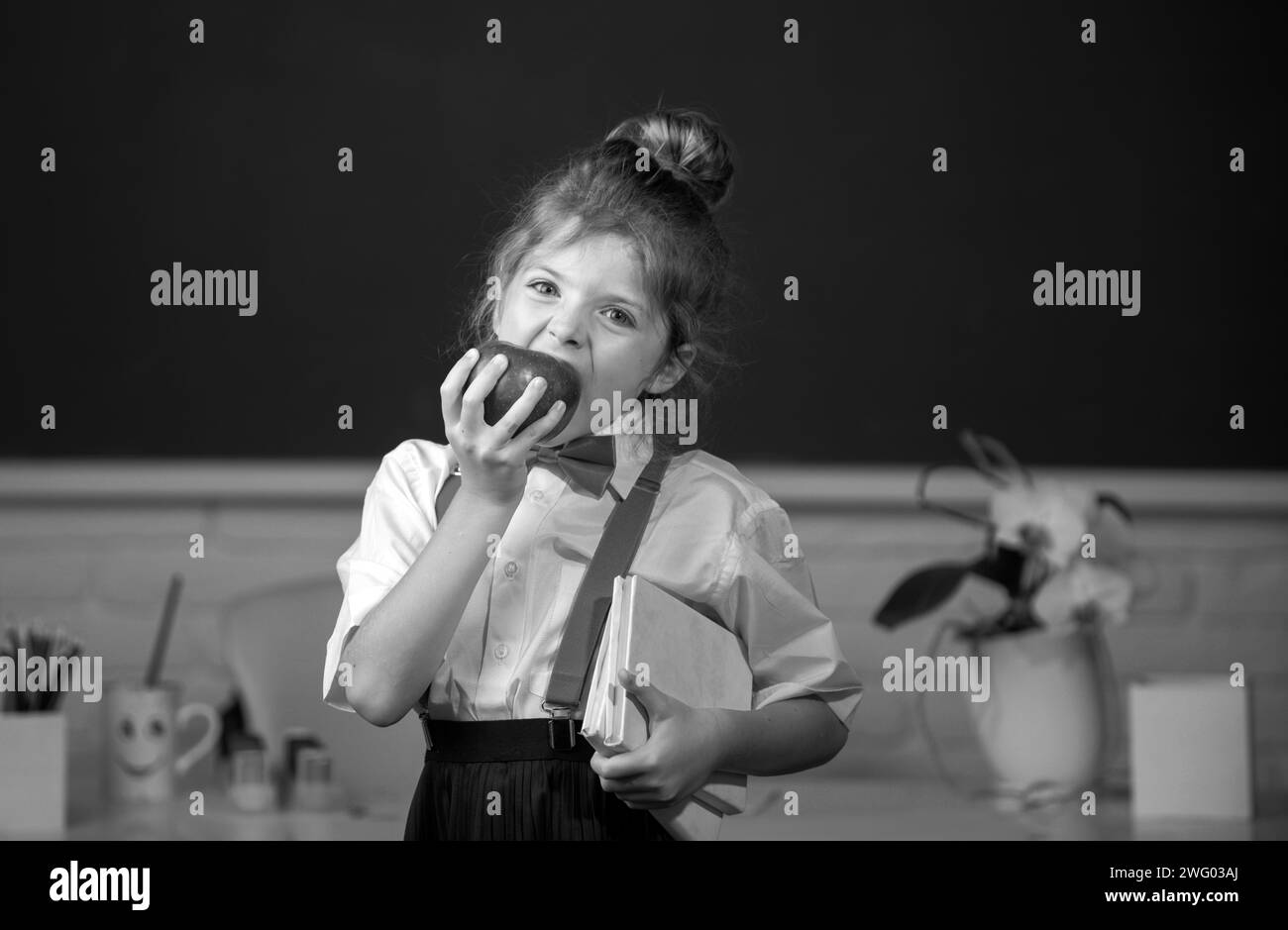 Little schoolgirl pupil student in class, eating apple at school. Back ...