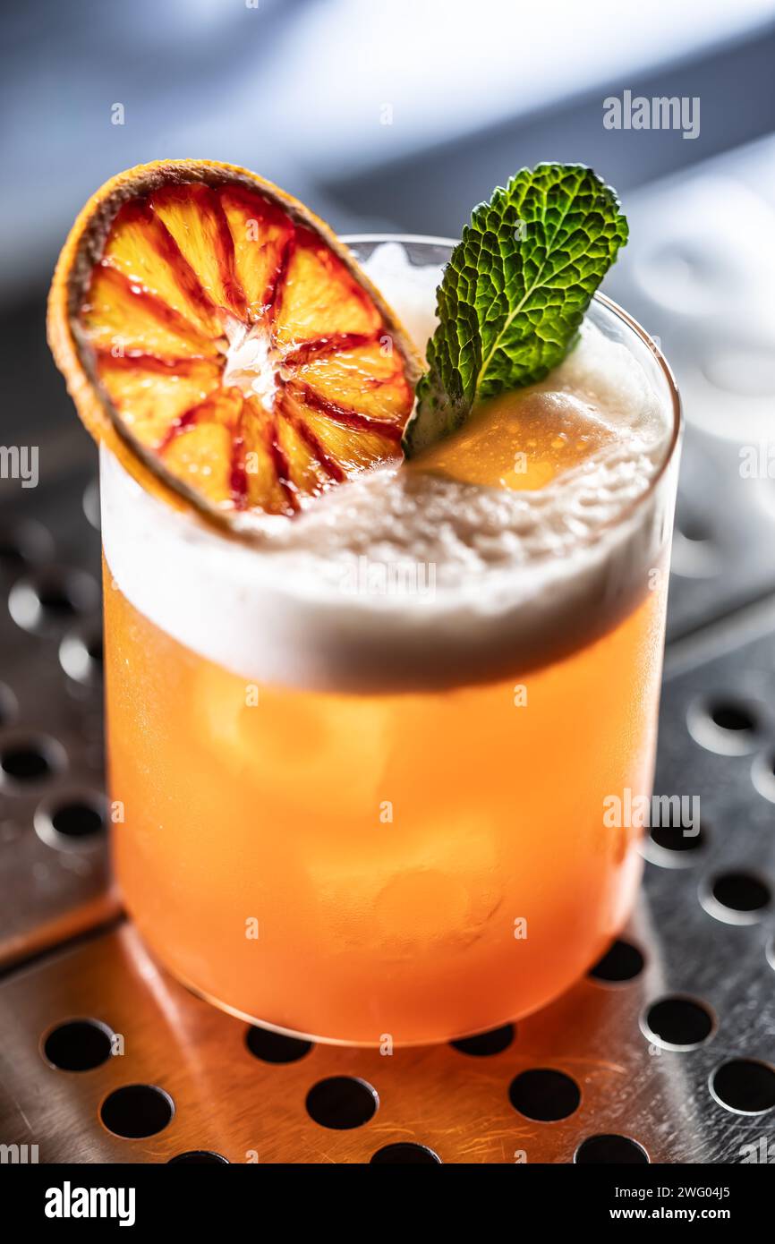 Glass of Jungle Bird cocktail garnished with dried red orange and mint ...