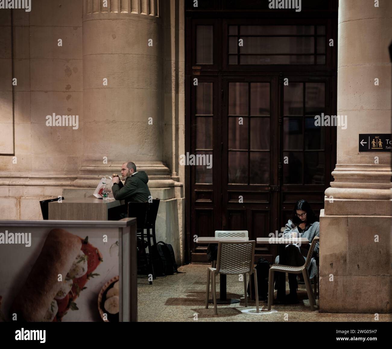 Two people, sit in their own little world inside Bordeaux train station ...