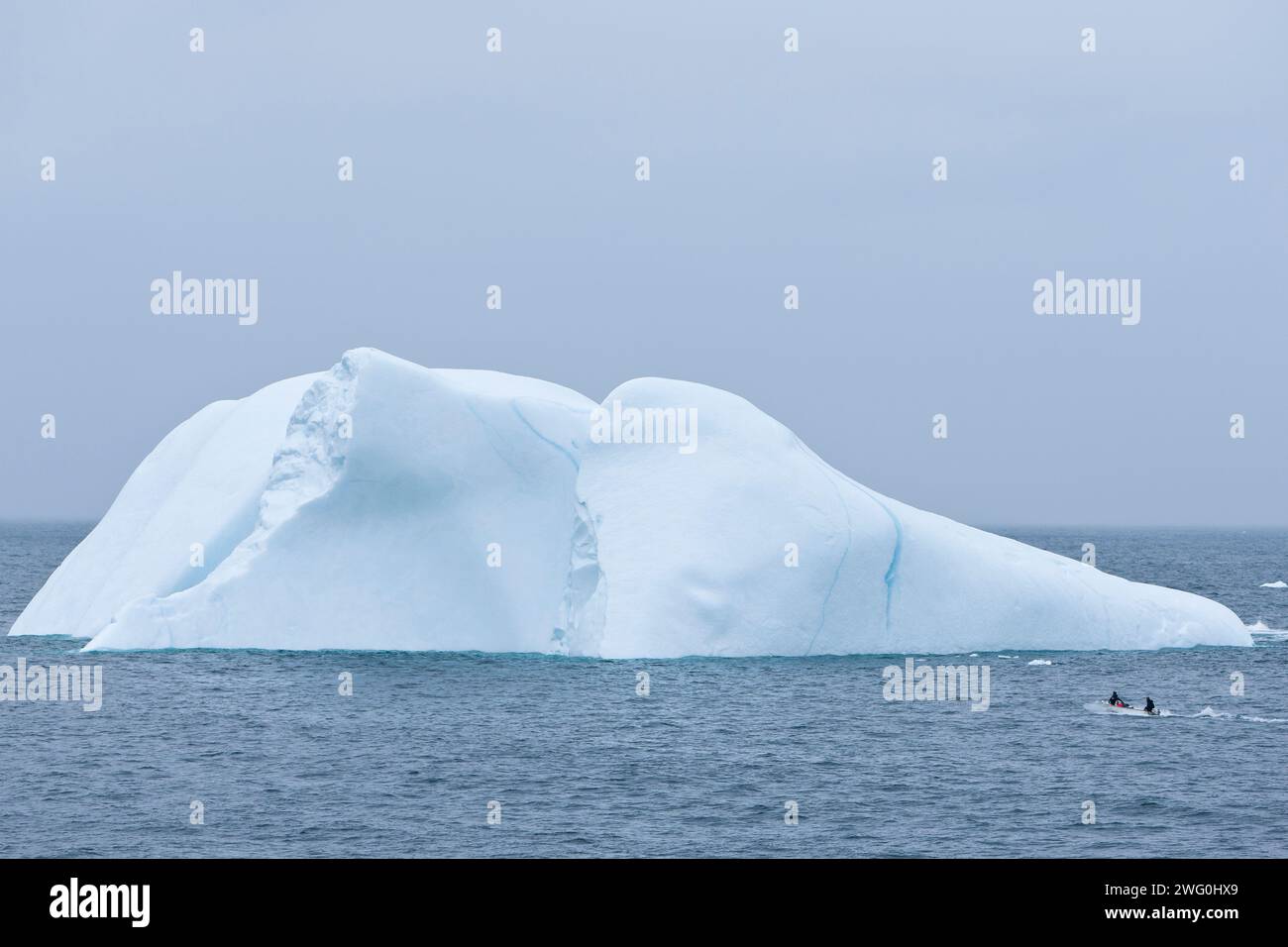 A small fishing boat motors past an iceberg on Greenland's east coast ...