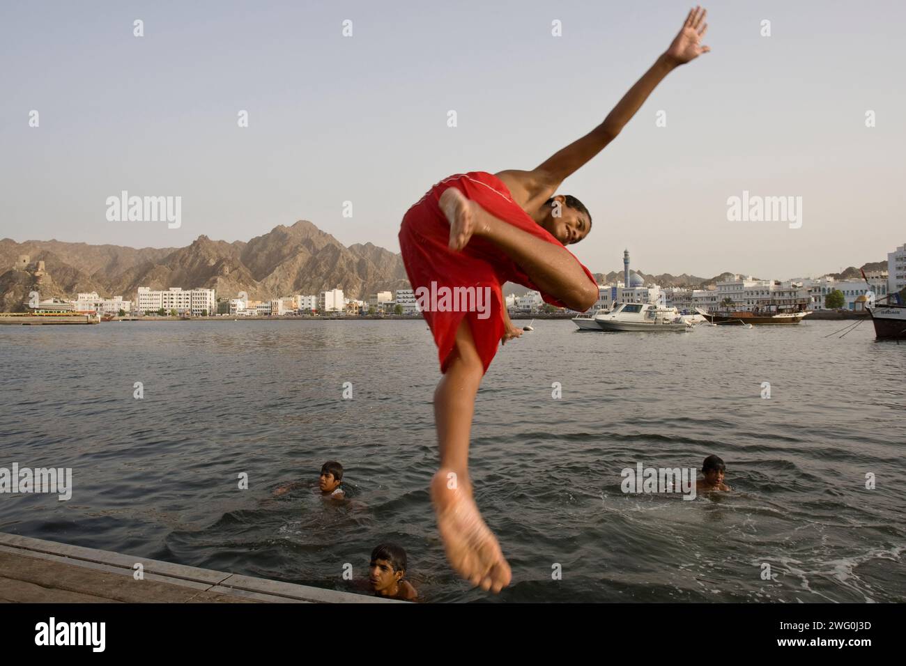 A boy dives into the water of Sultan Qaboos Port in Muscat, Oman Stock ...