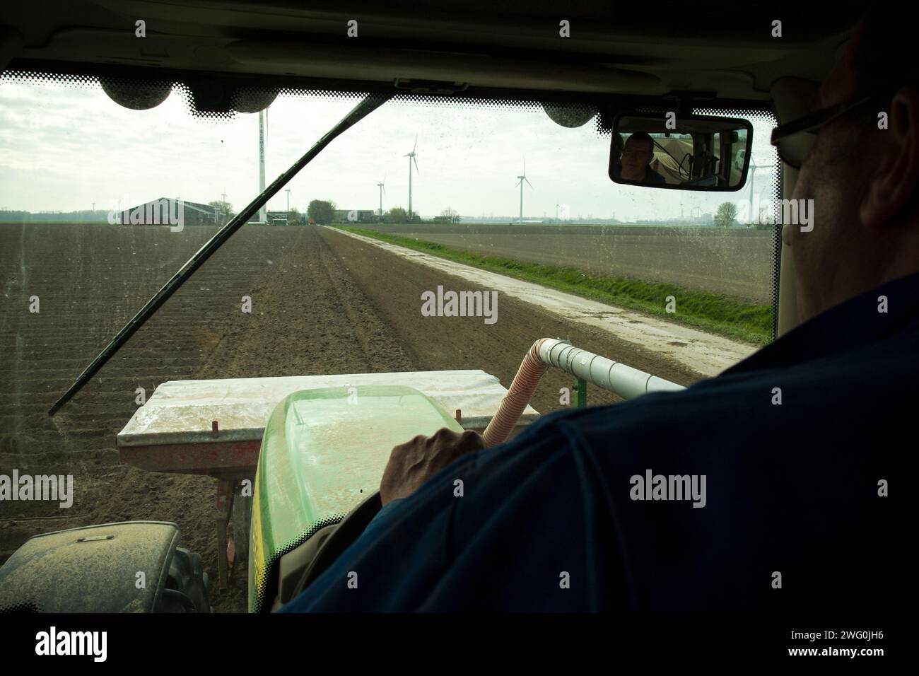Dutch farmer driving a potato seeder with wind turbines in background ...