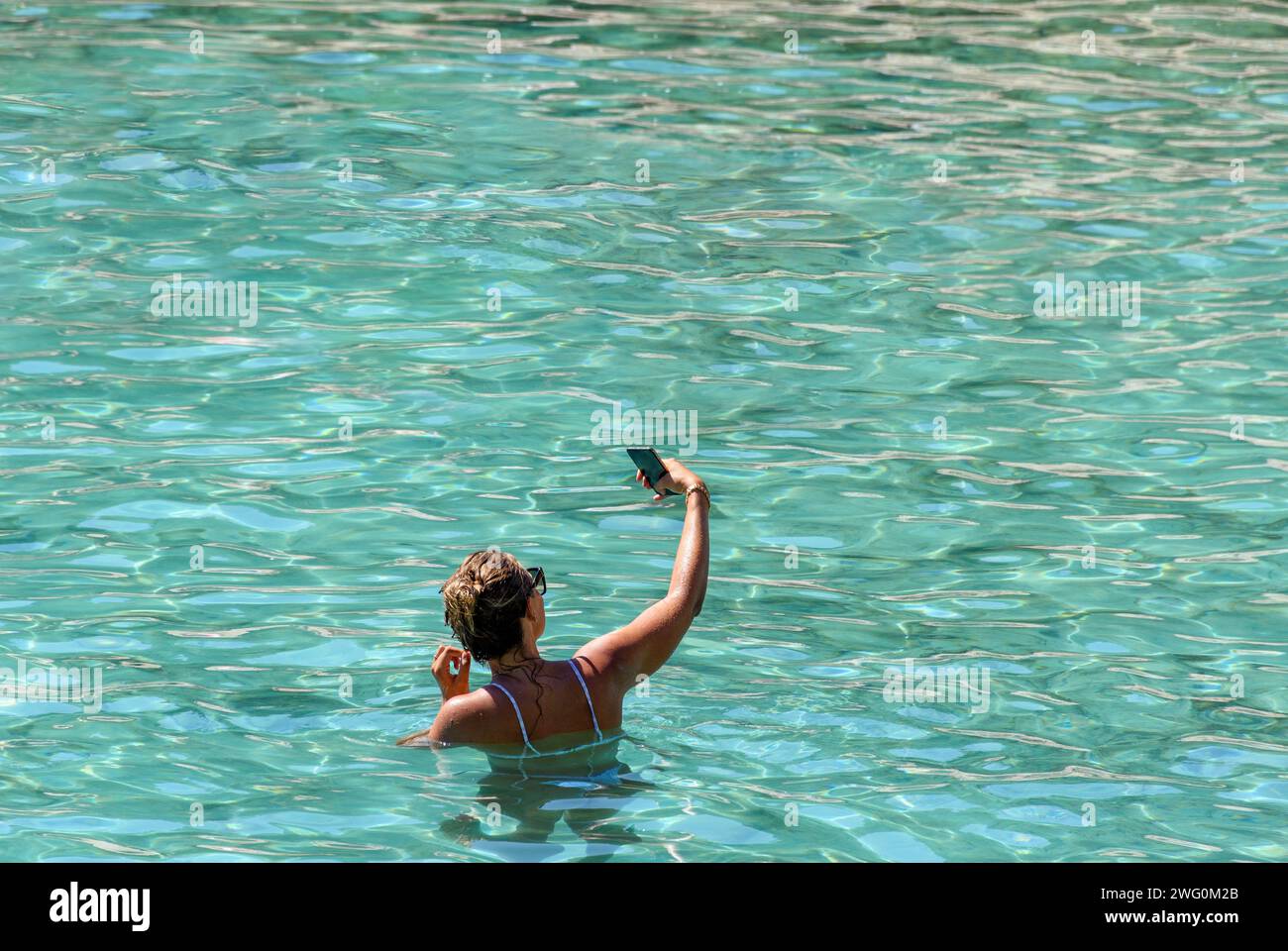 Rear view of woman taking a selfie in turquoise sea during summer ...