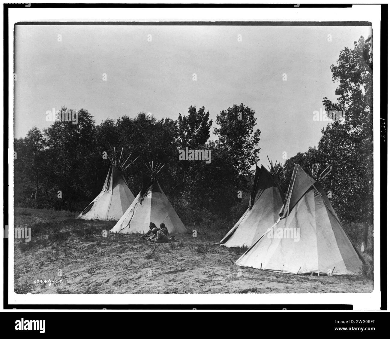 An Assiniboin camp containing four tepees with Indians seated on ground ...