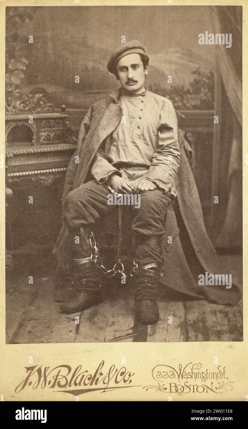 Full-length portrait of a man in convict clothing and leg irons, seated ...