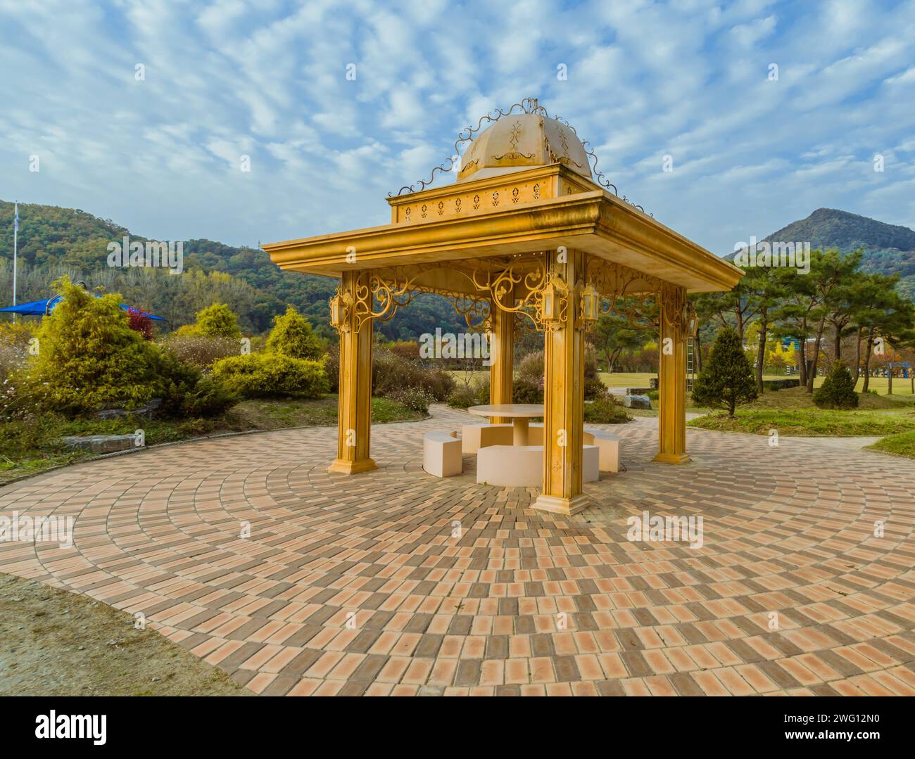 Golden colored gazebo with lush foliage with a flag pole behind a blue ...