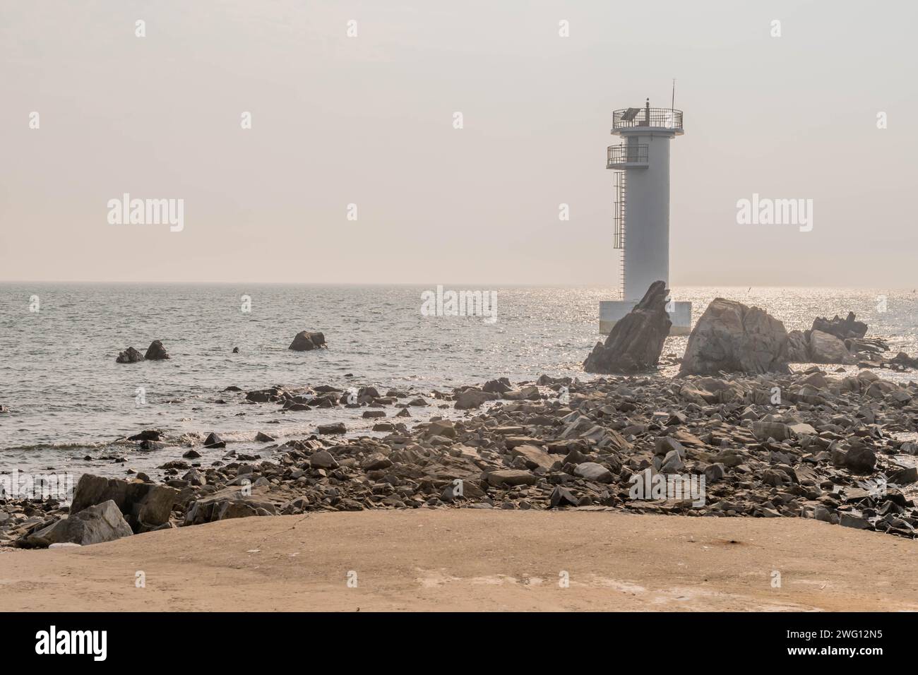 White lighthouse located at rocky point on seashore with sun sparkling ...