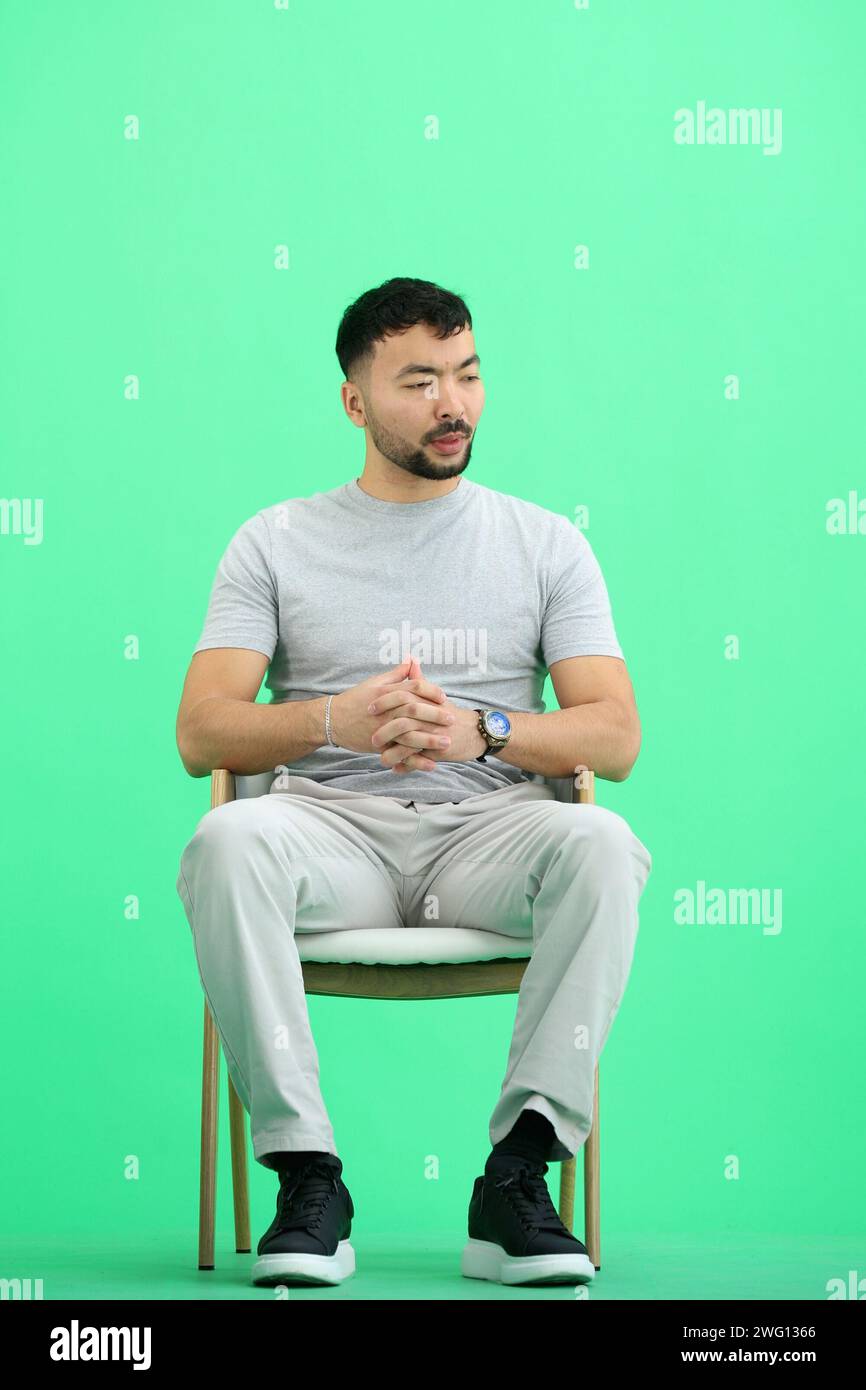 A man, on a green background, in full height, sitting on a chair Stock ...
