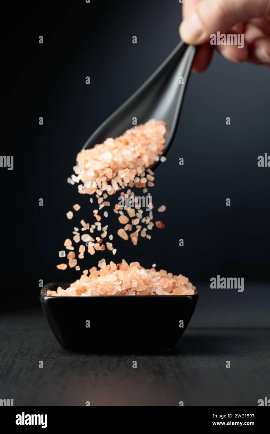Pink salt is poured into a small black bowl. Himalayan salt on a black ...