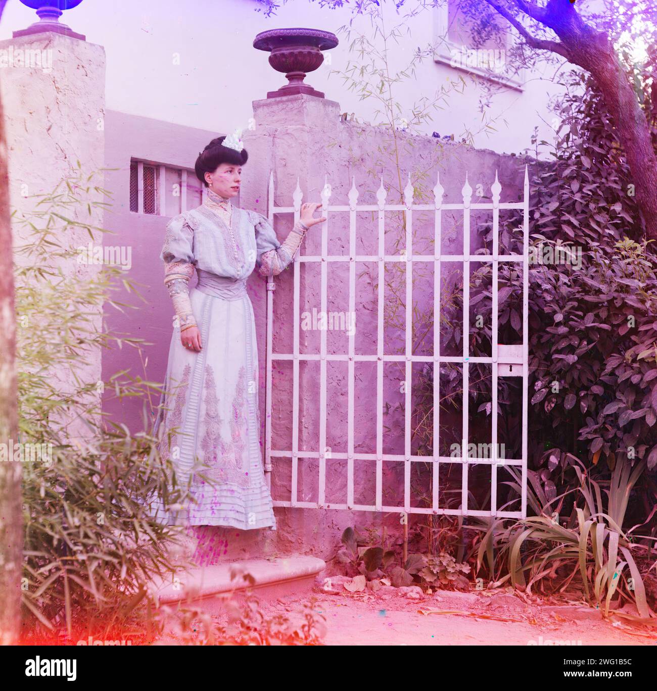 In Italy, between 1905 and 1915. Woman in formal dress, posed, standing near gate Stock Photo ...