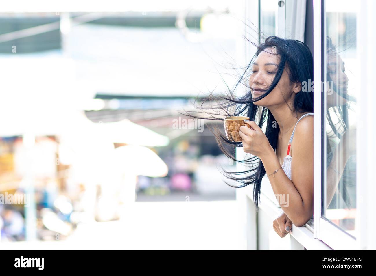 A dreamy woman holds a mug in an open window of a residential building ...