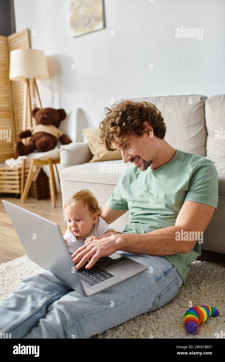 happy father using laptop near infant son in living room, balancing ...