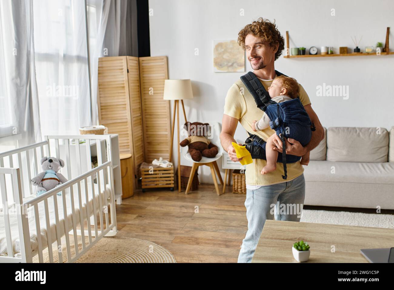 happy father with infant son in carrier holding yellow rag near working ...