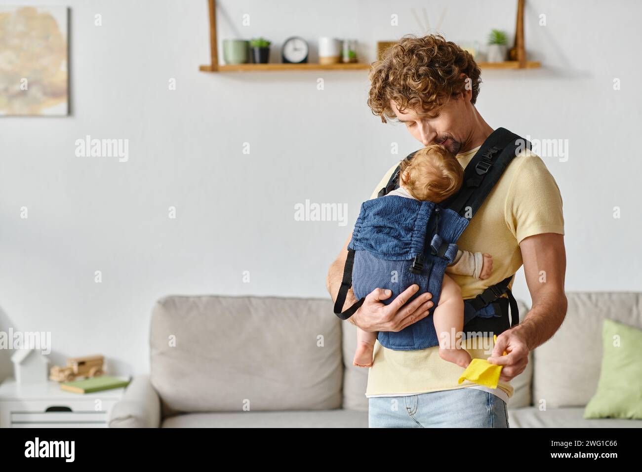 happy father kissing sleeping infant son in carrier and holding yellow ...