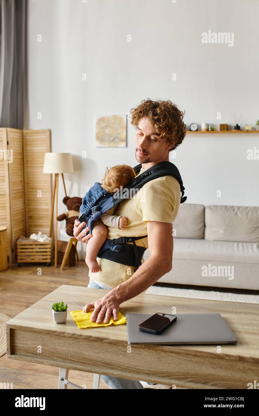 busy father with infant son in carrier wiping table with yellow rag ...