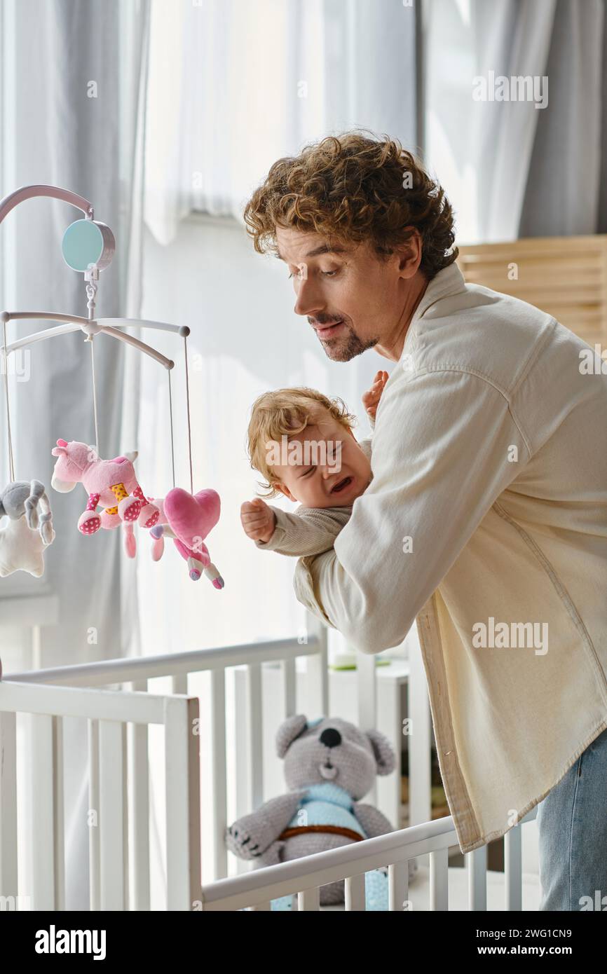 caring single father holding his crying infant son near baby crib in ...