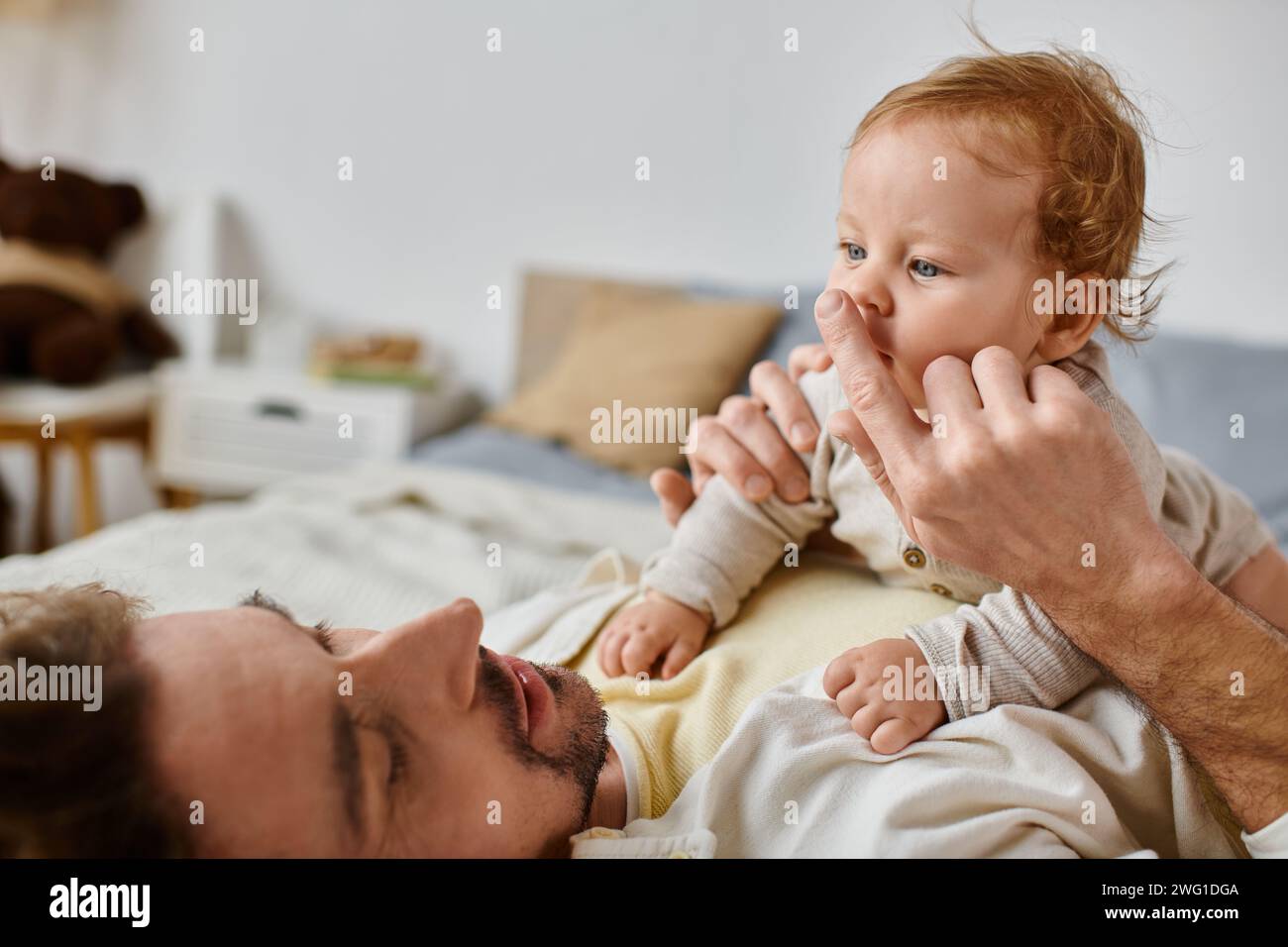 man with curly hair and beard touching nose of his infant son, bond ...