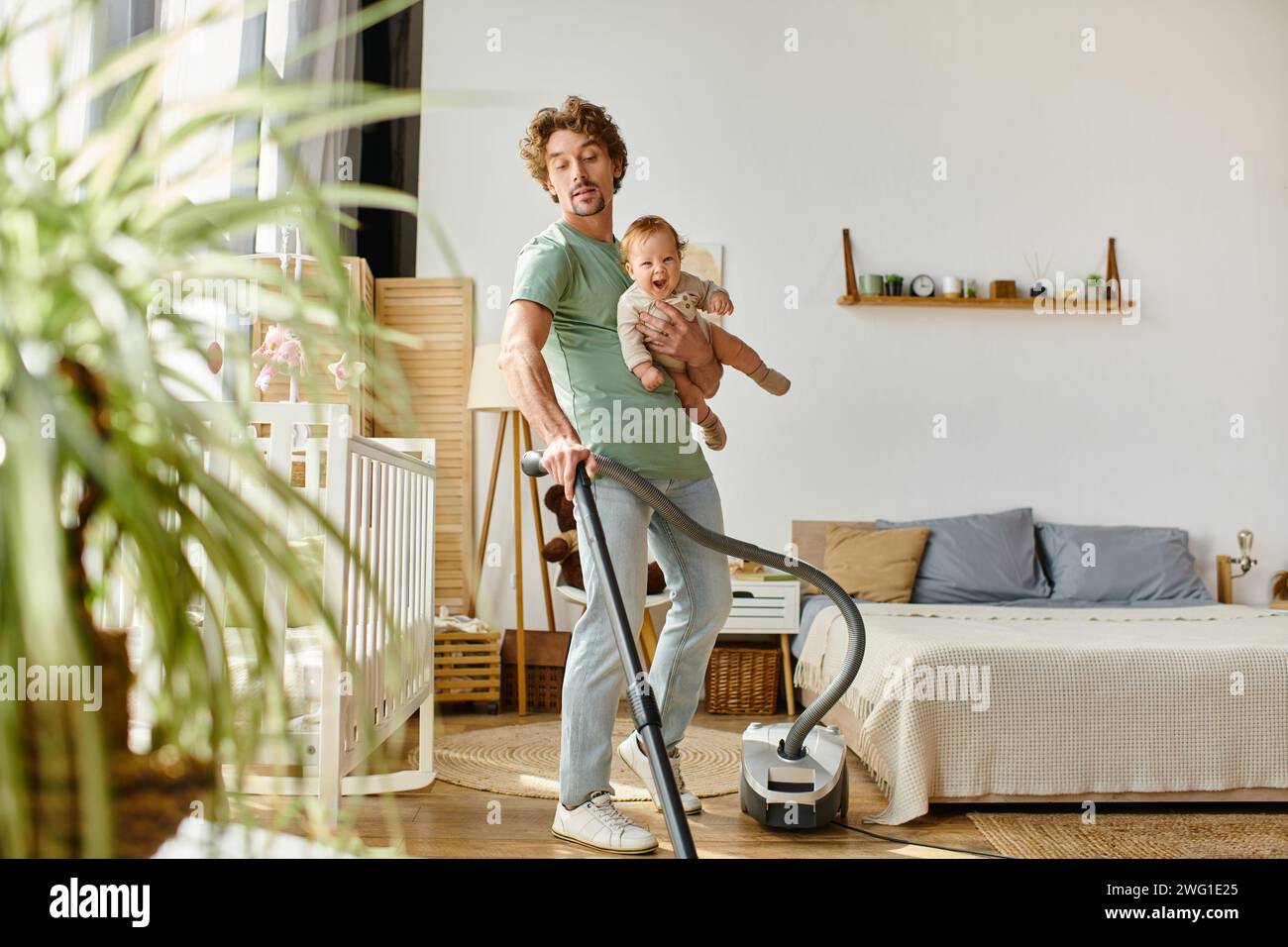 man multitasking housework and childcare, curly father vacuuming ...