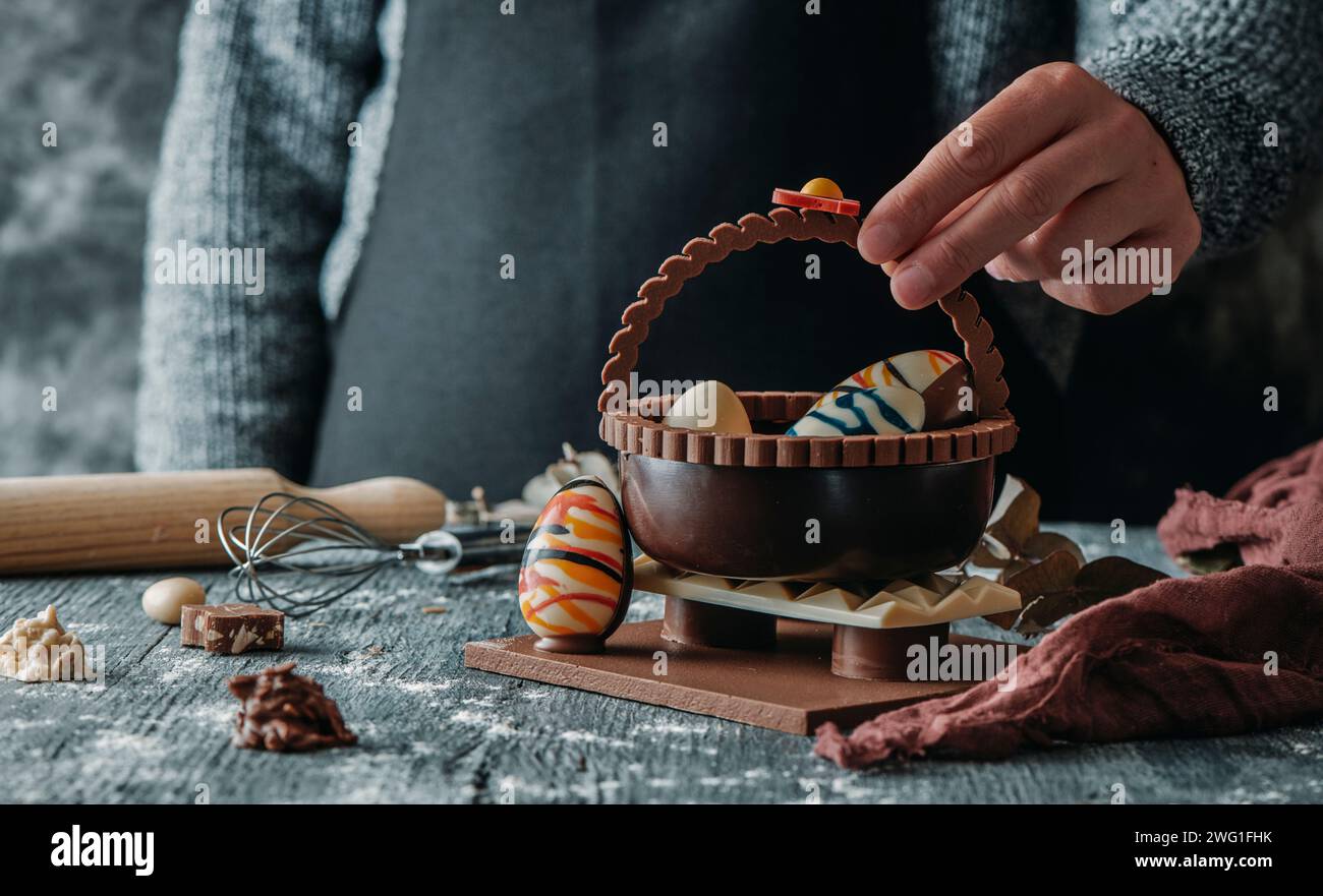 man, wearing a black apron, holds a chocolate basket with some ...