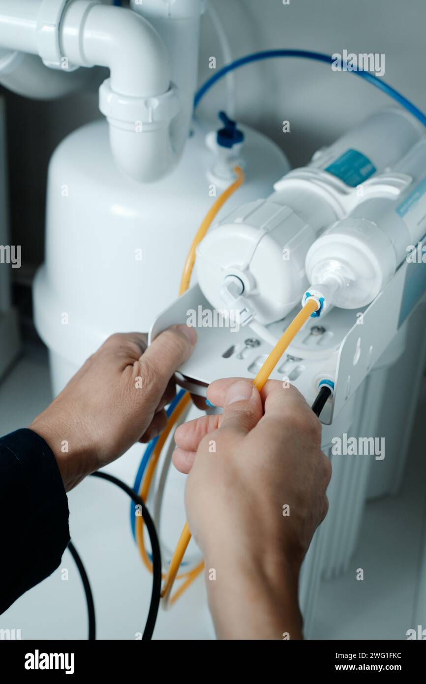 a caucasian man, in blue overalls, installs a domestic reverse osmosis ...