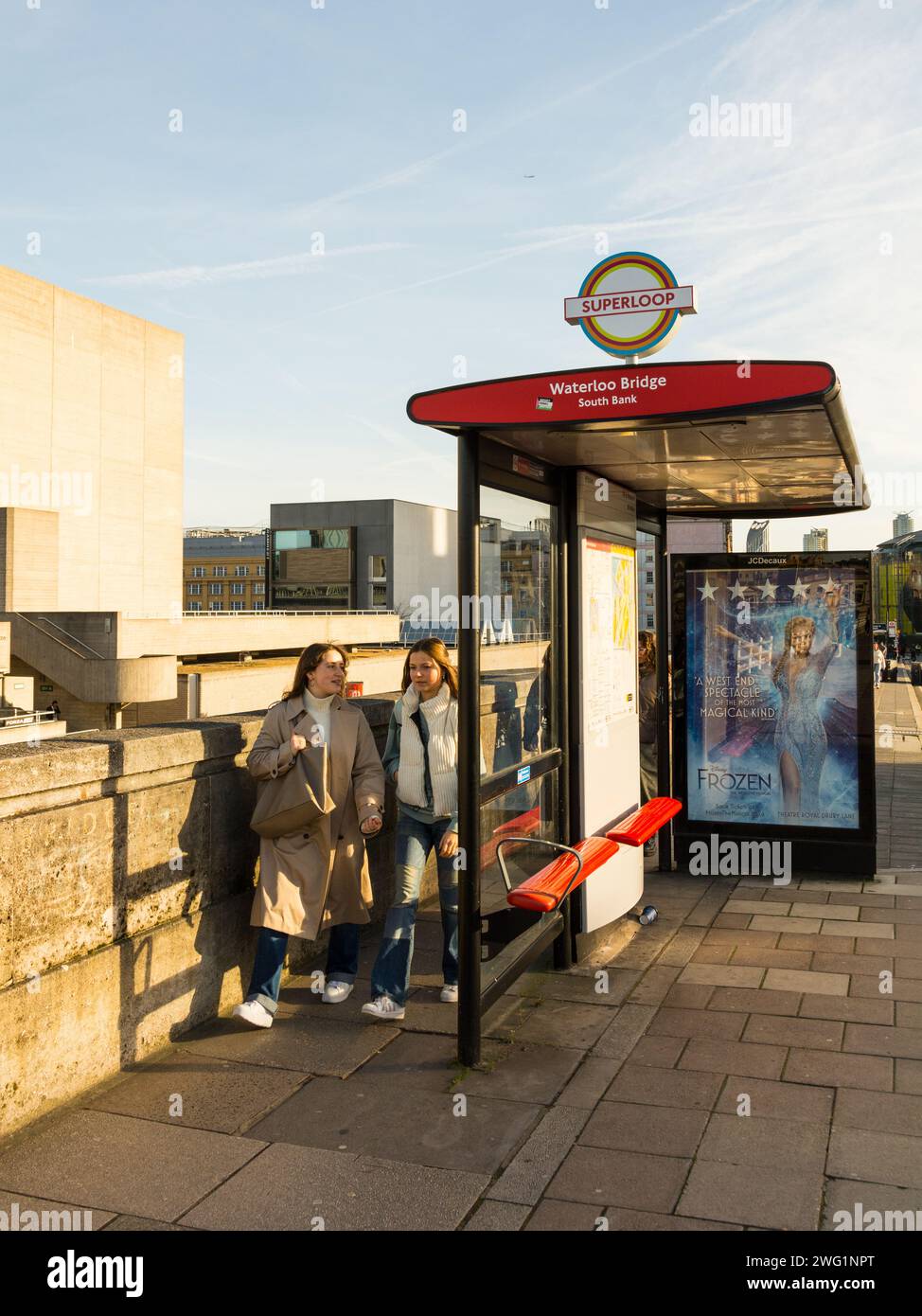 Two women walking past a colourful Superloop Roundel on Waterloo Bridge ...
