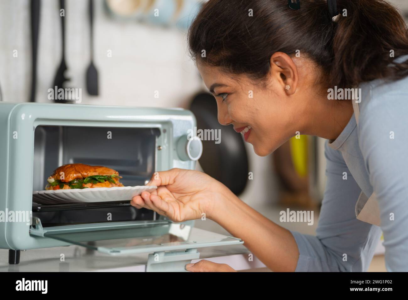 Happy Indian woman cooking burger by placing it on microwave oven at ...
