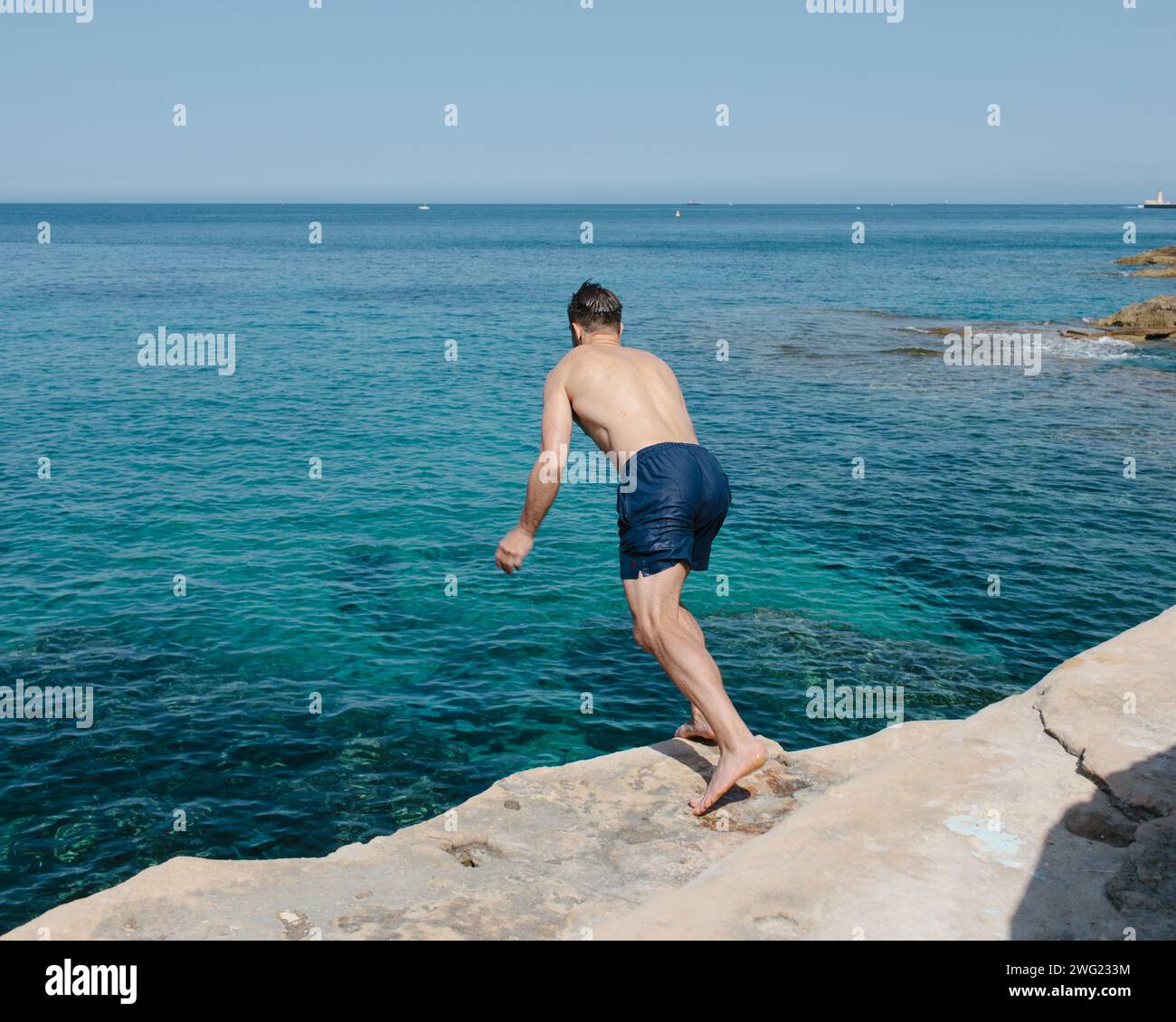 A man jumps into the sea from the rocks on a private beach in Valetta ...