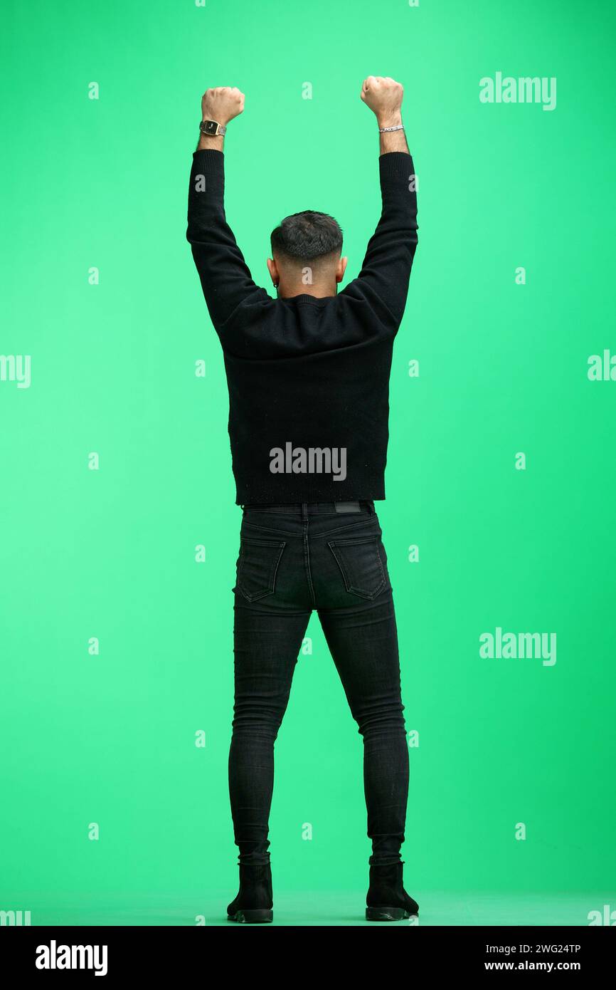 A man, full-length, on a green background, raised his hands up Stock ...