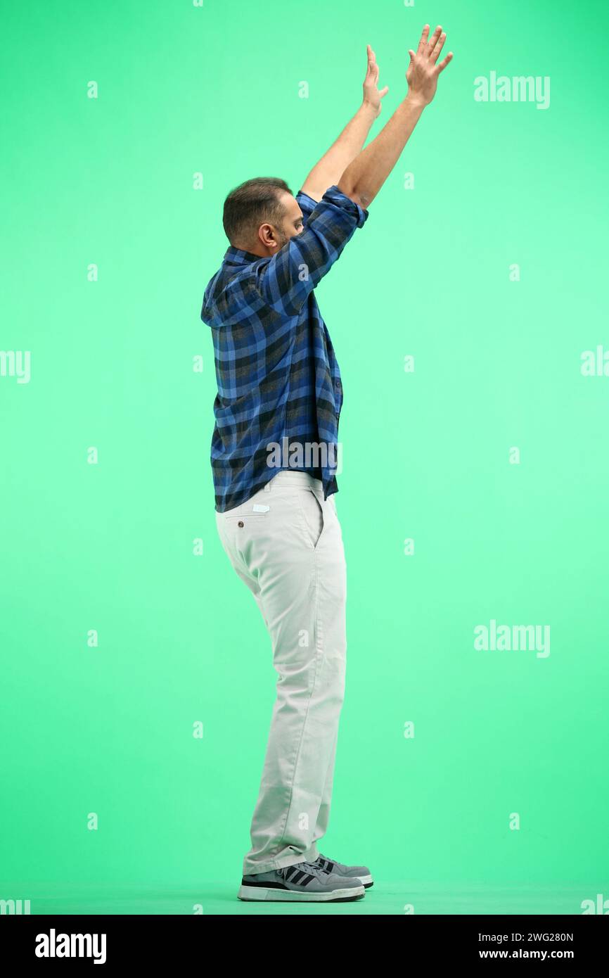 A man, full-length, on a green background, raised his hands up Stock ...