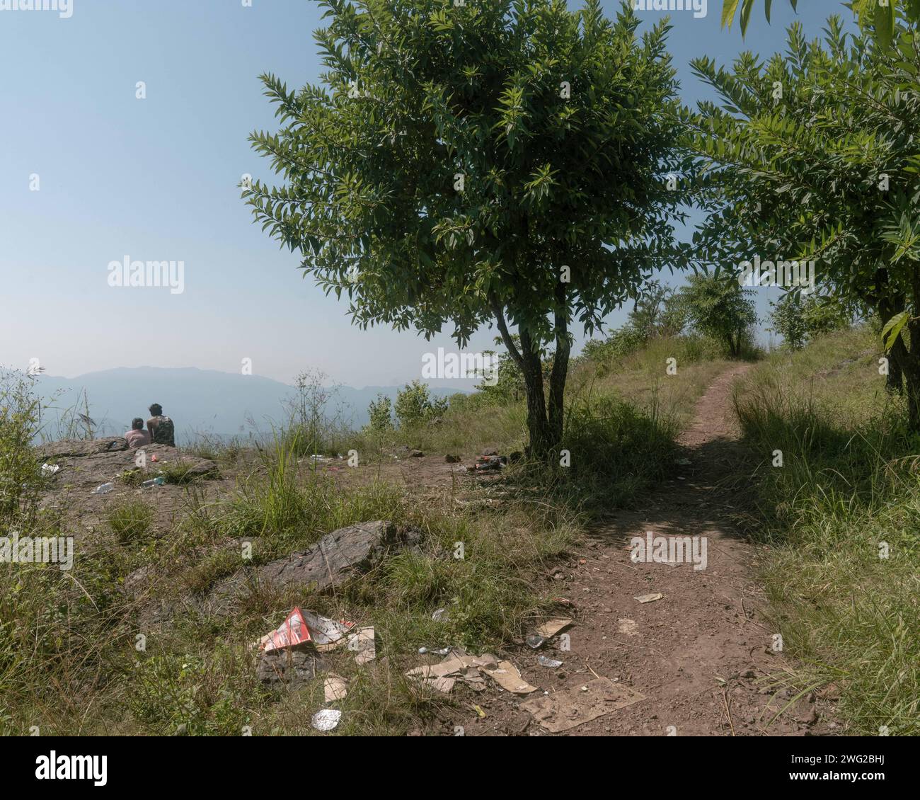 A Nepali couple sits at a trash-covered viewpoint looking over a valley ...