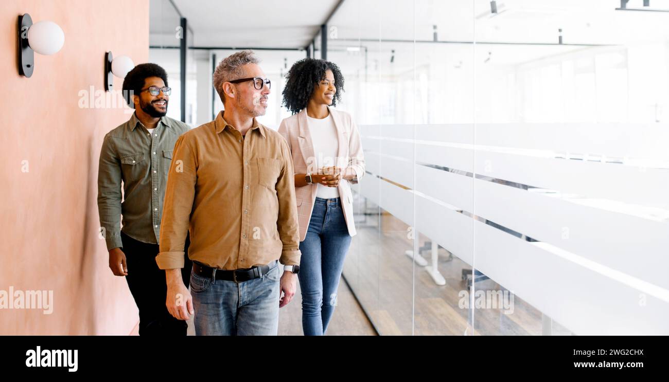 Three colleagues walk through their office space, engaged in a casual ...