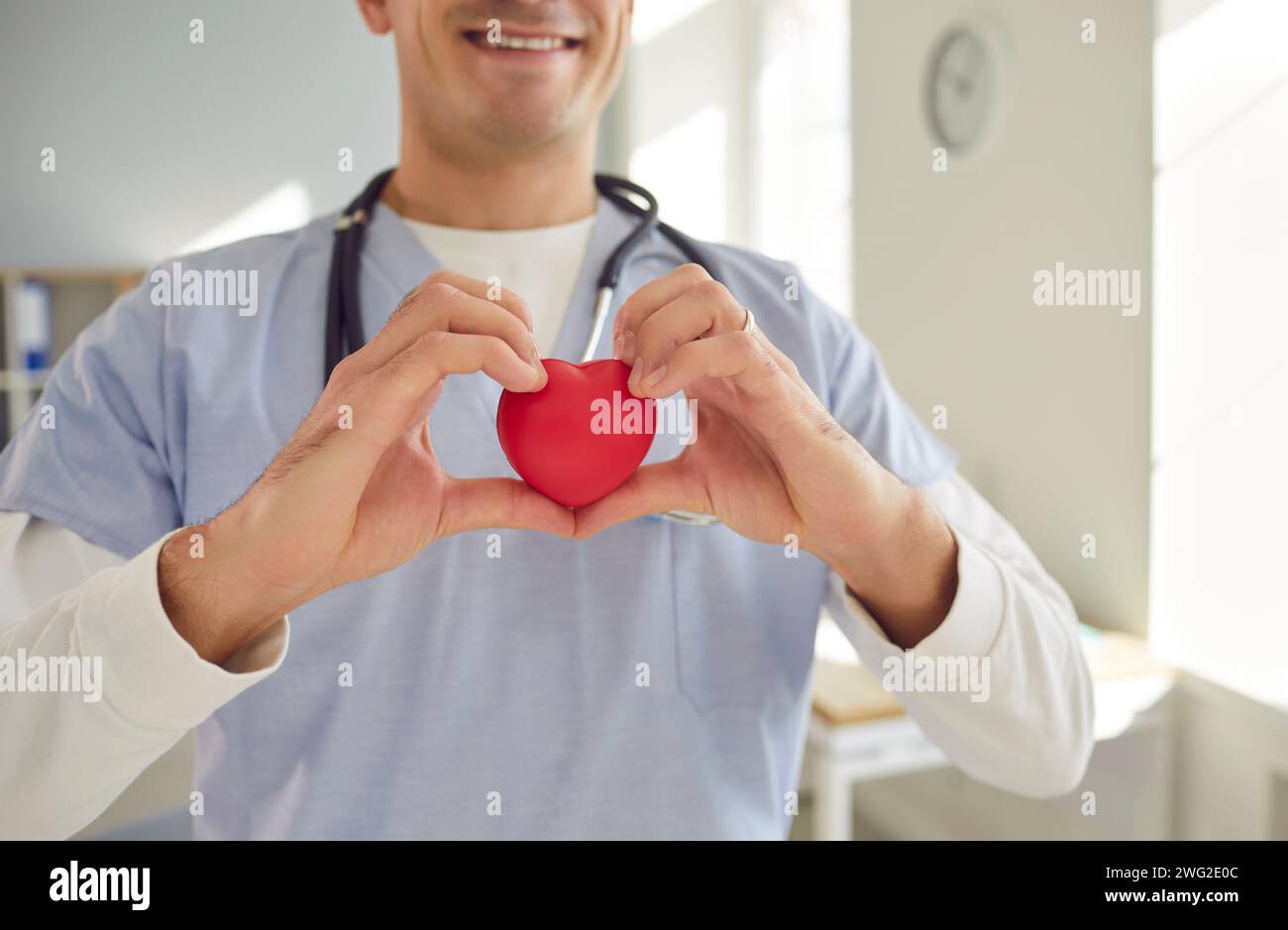 Male smiling man doctor cardiologist in blue uniform holding red heart ...
