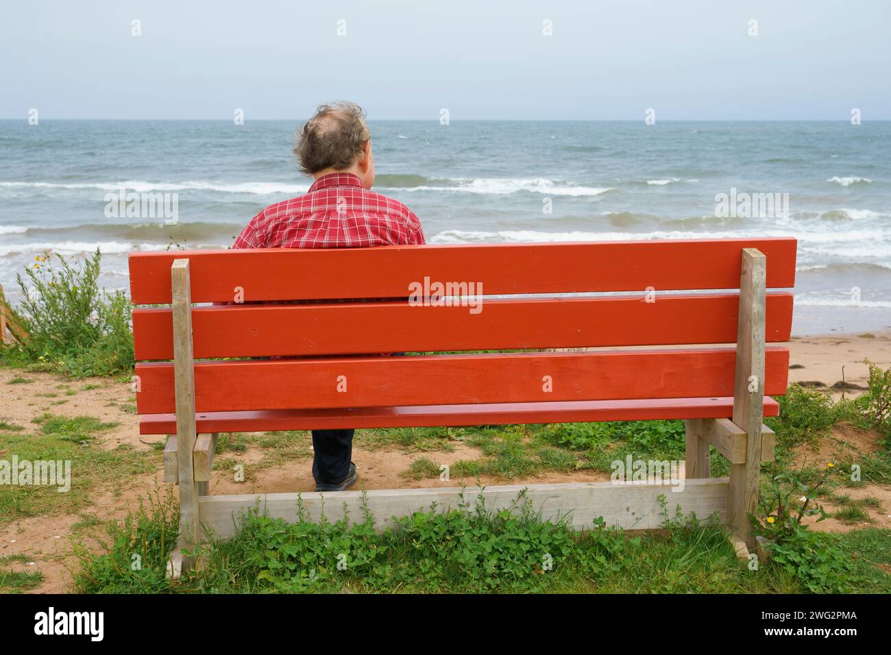 Older man sitting on a bench by the Atlantic ocean in Prince Edward ...