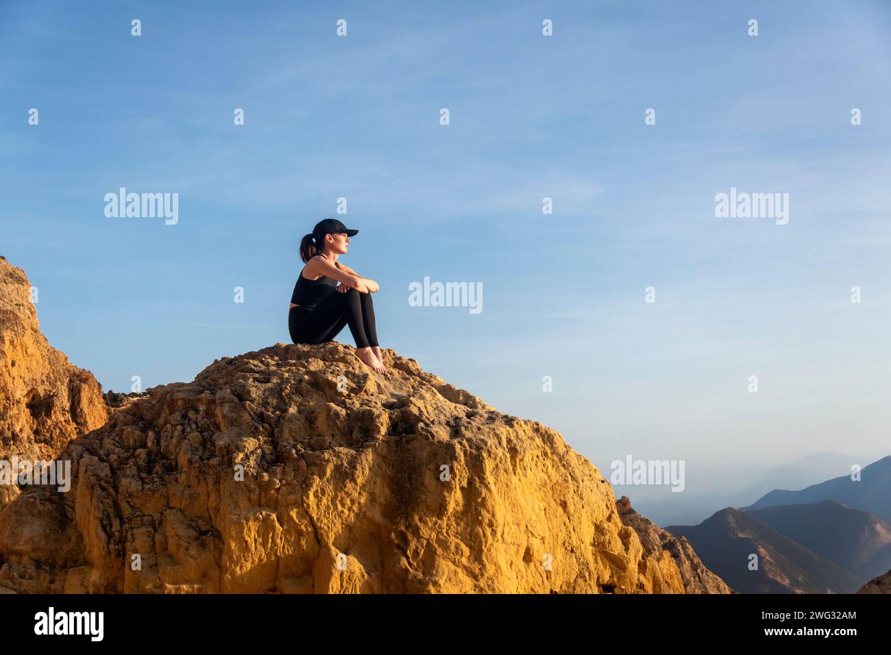 Sporty woman sitting on top of a rock looking at the view of mountains ...