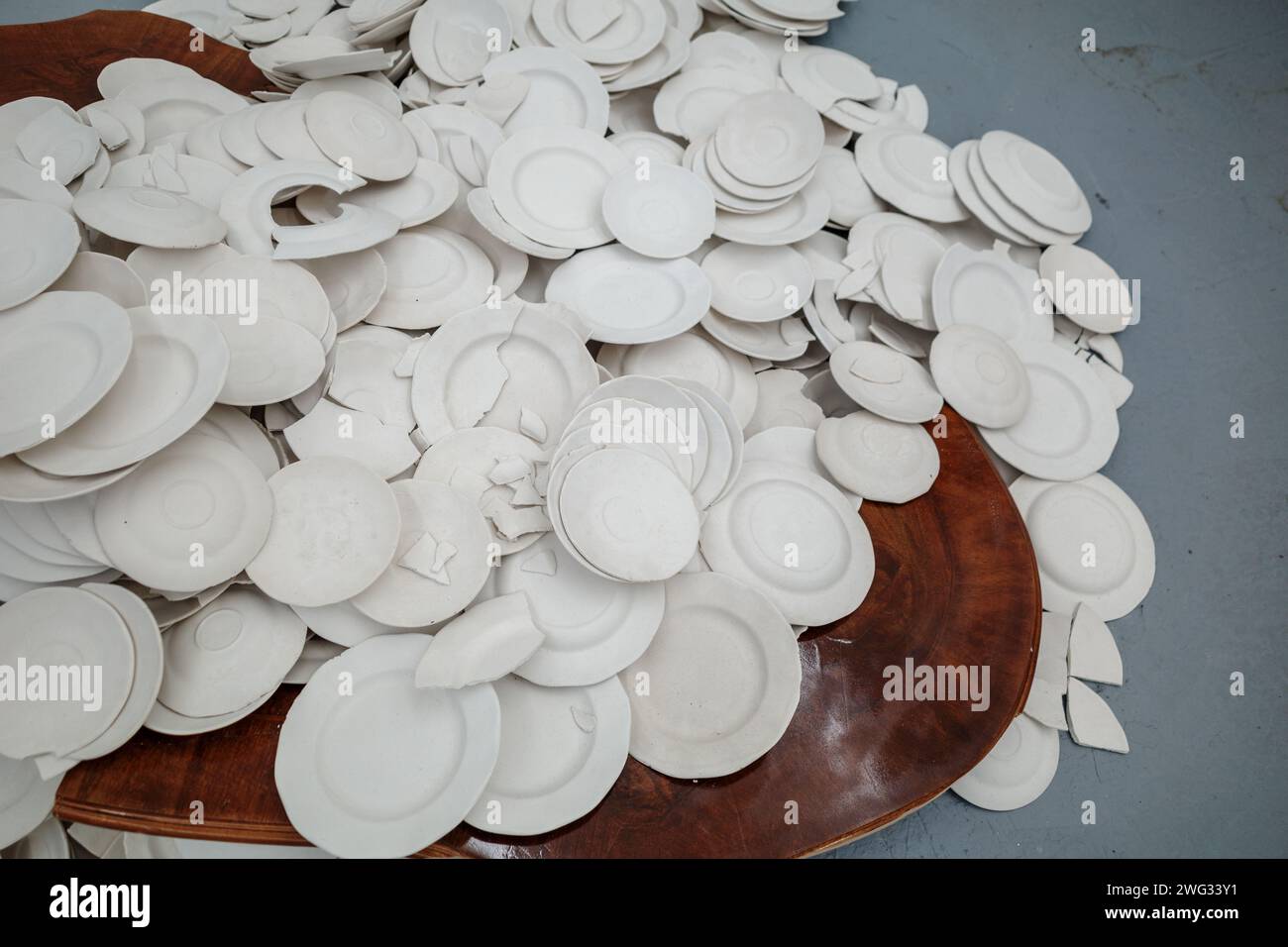 A pile of white, unfinished ceramic plates at various stages of the ...