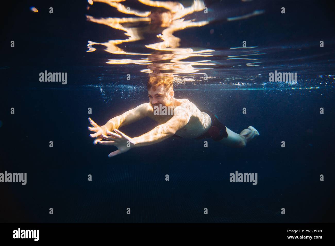 A handsome young man swims underwater in a swimming pool while on ...